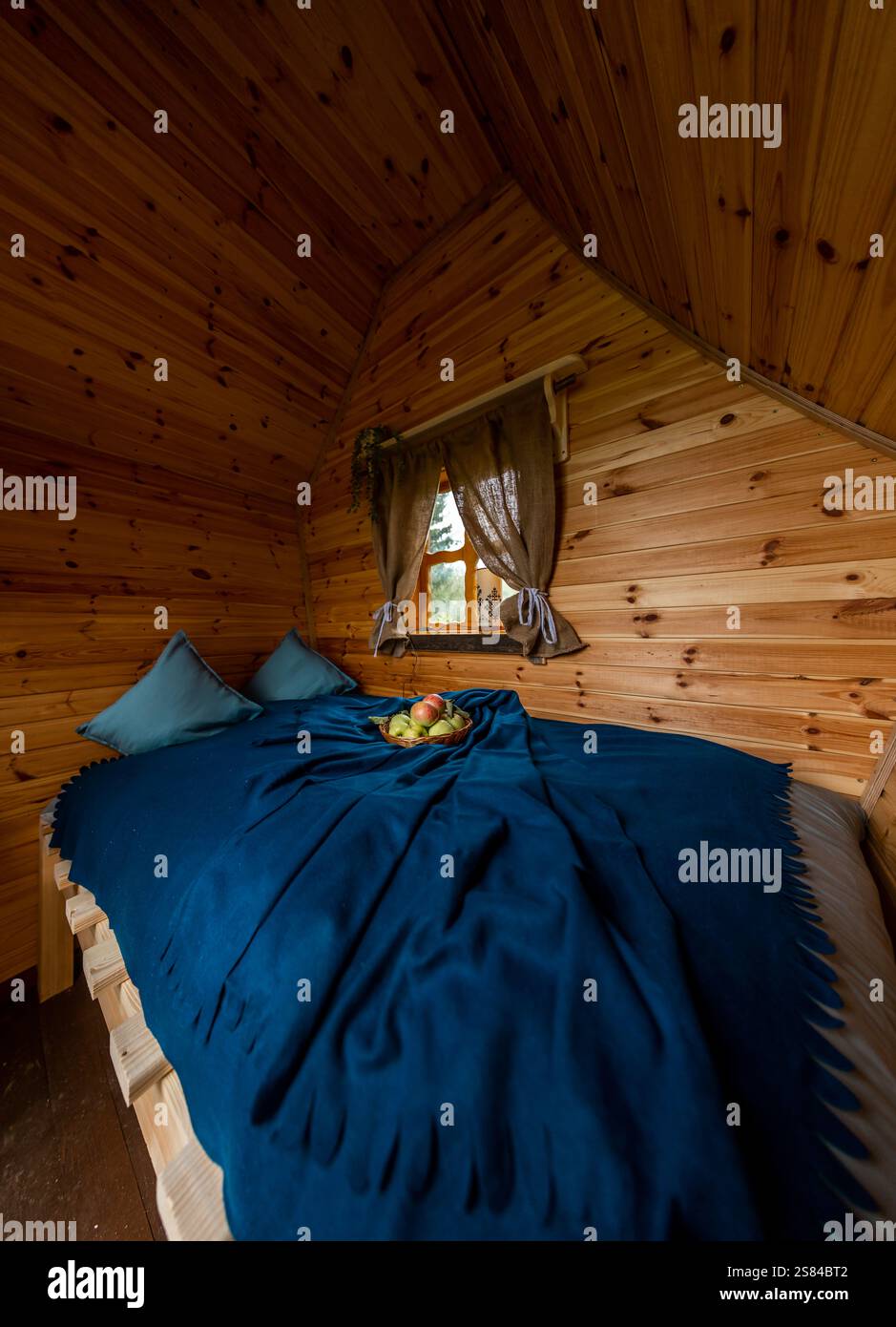 Compact wooden cabin interior with polished pine walls, a bed with blue ...
