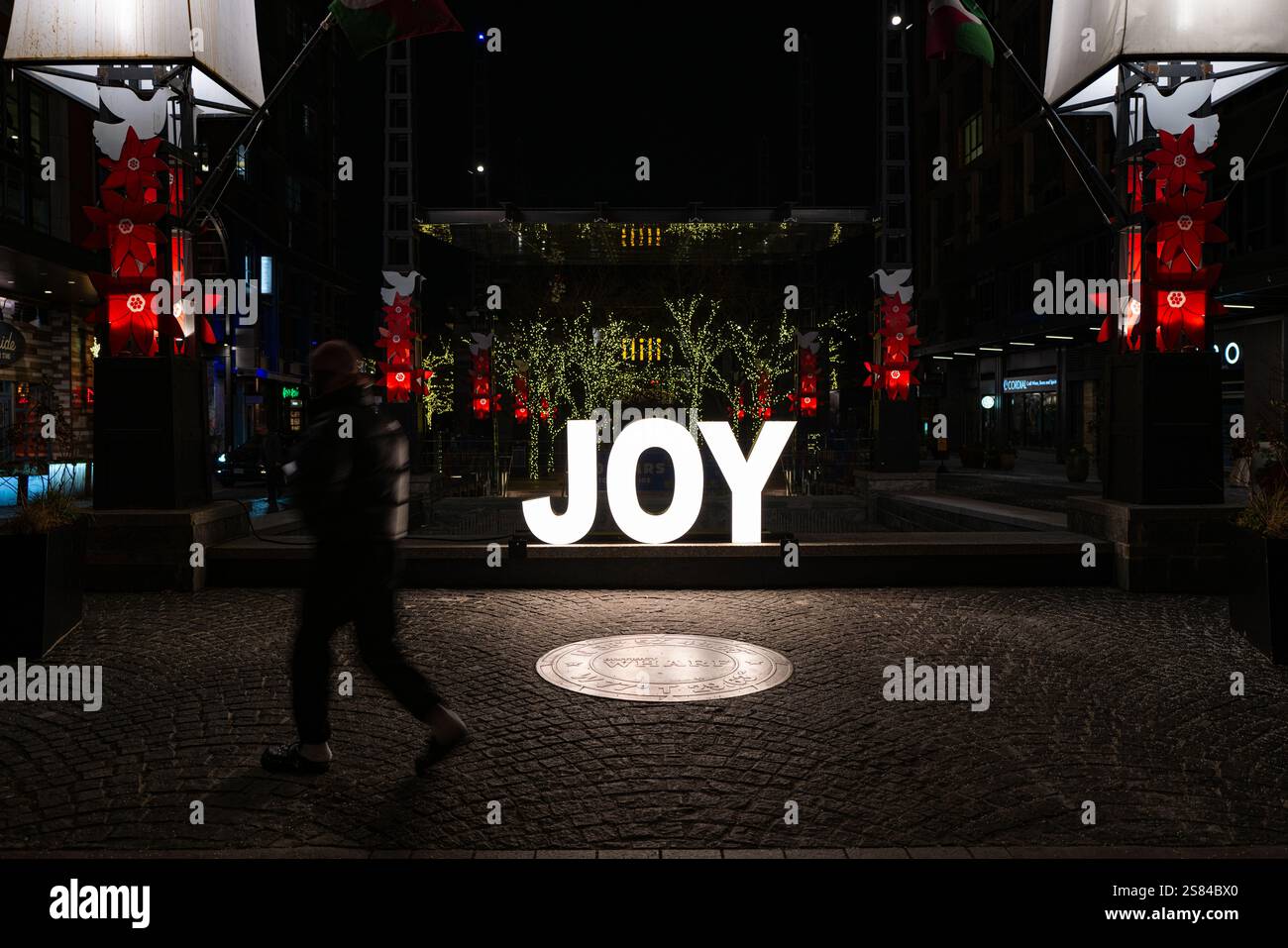 Night photo of a man walking past the lit Joy sign at the entrance to ...