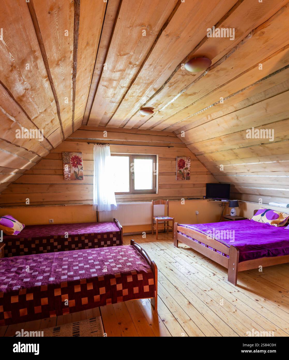 Rustic attic bedroom with polished wooden ceilings, three beds, a small ...