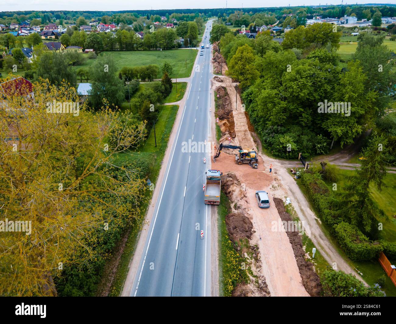 Road construction site along a two lane road with an excavator digging ...