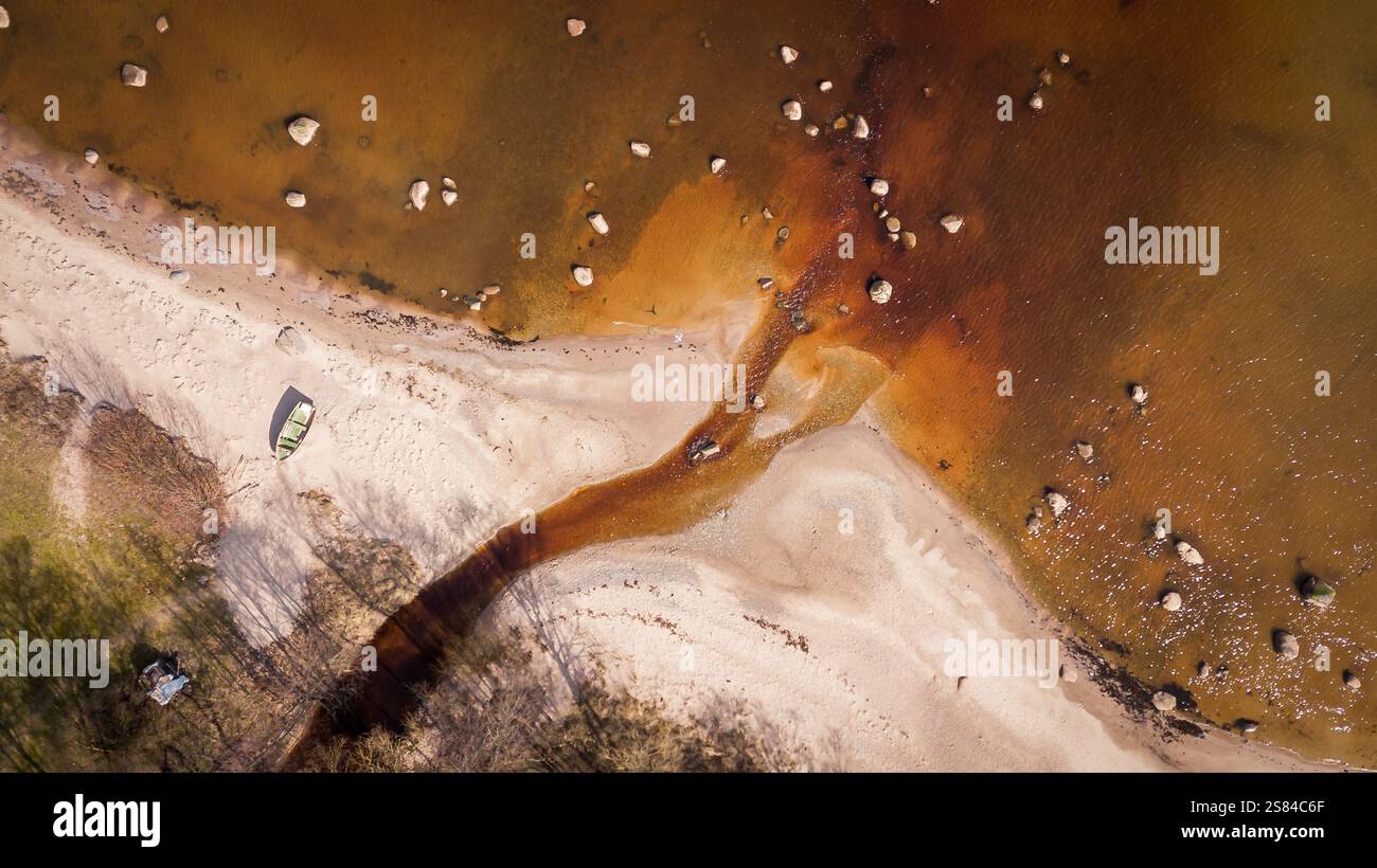 Aerial perspective of a sandy shoreline where a reddish brown stream ...
