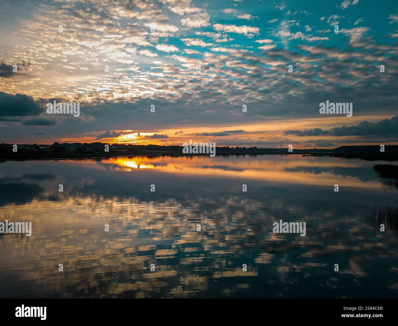 A colorful sunset with orange and blue tones reflects on calm water ...