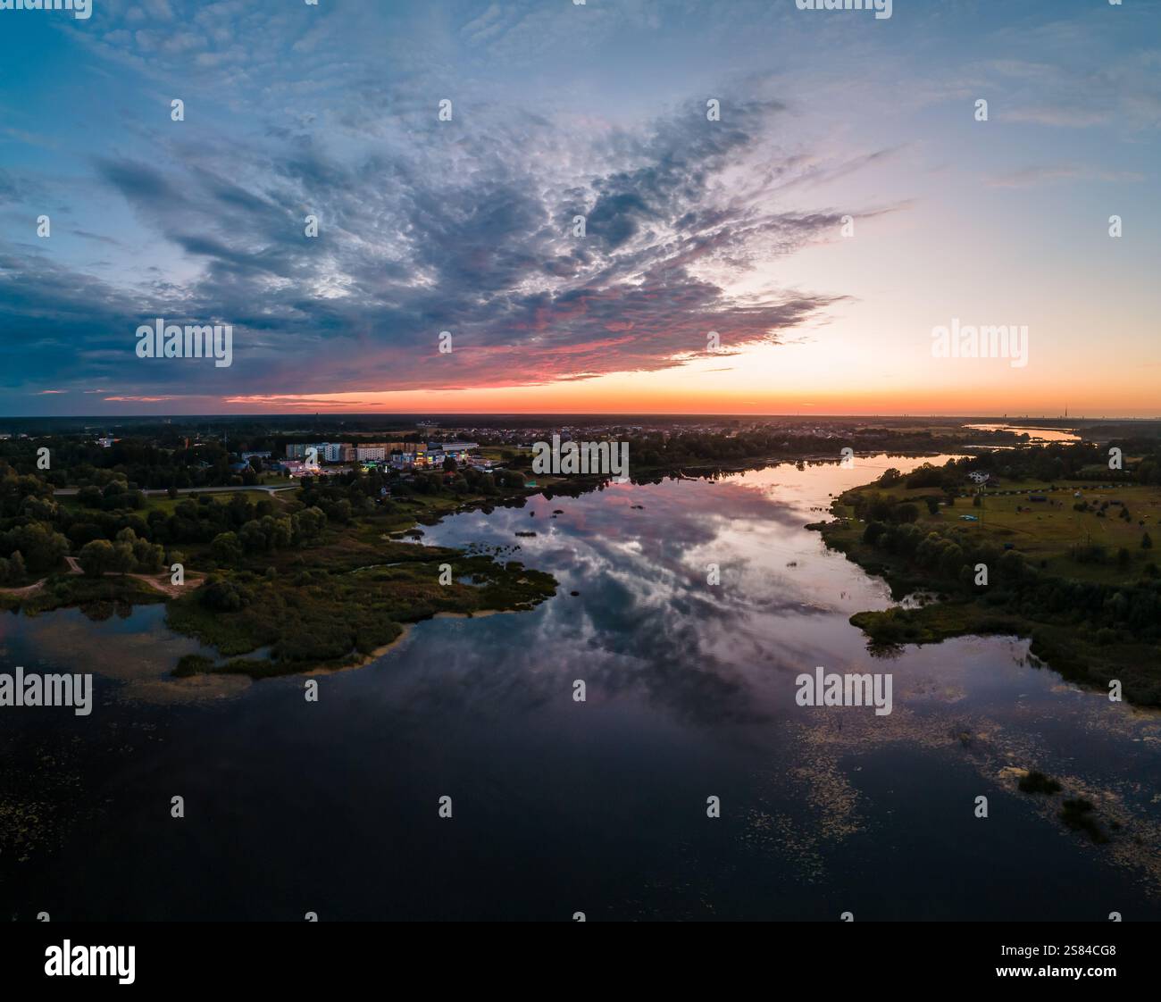 Wide aerial view of a calm river reflecting sunset hues, surrounded by ...