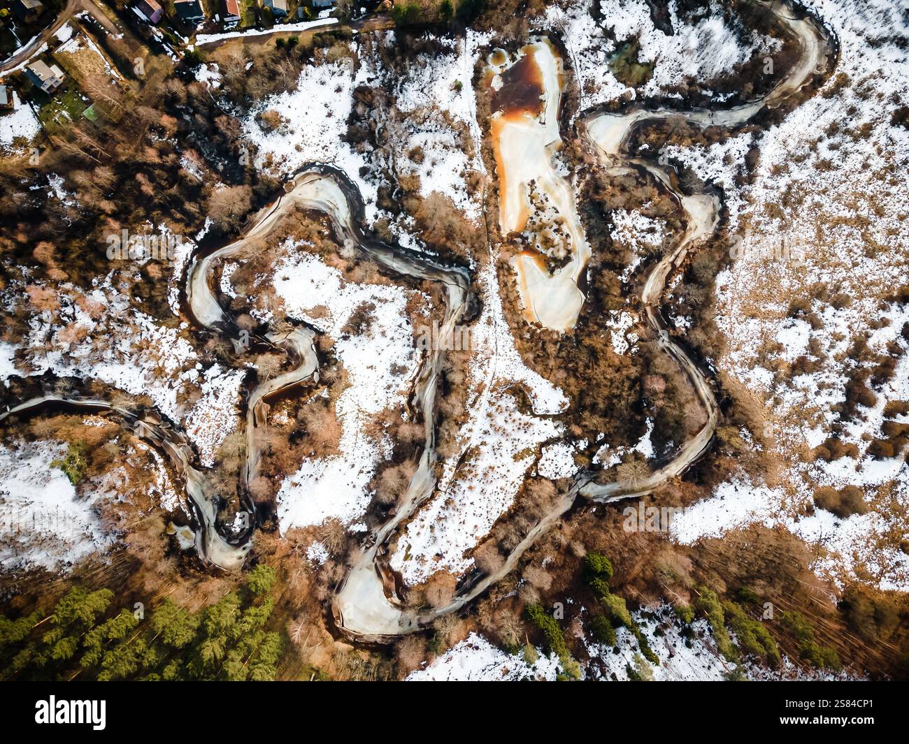 A narrow road curves through a snowy terrain with brown vegetation ...