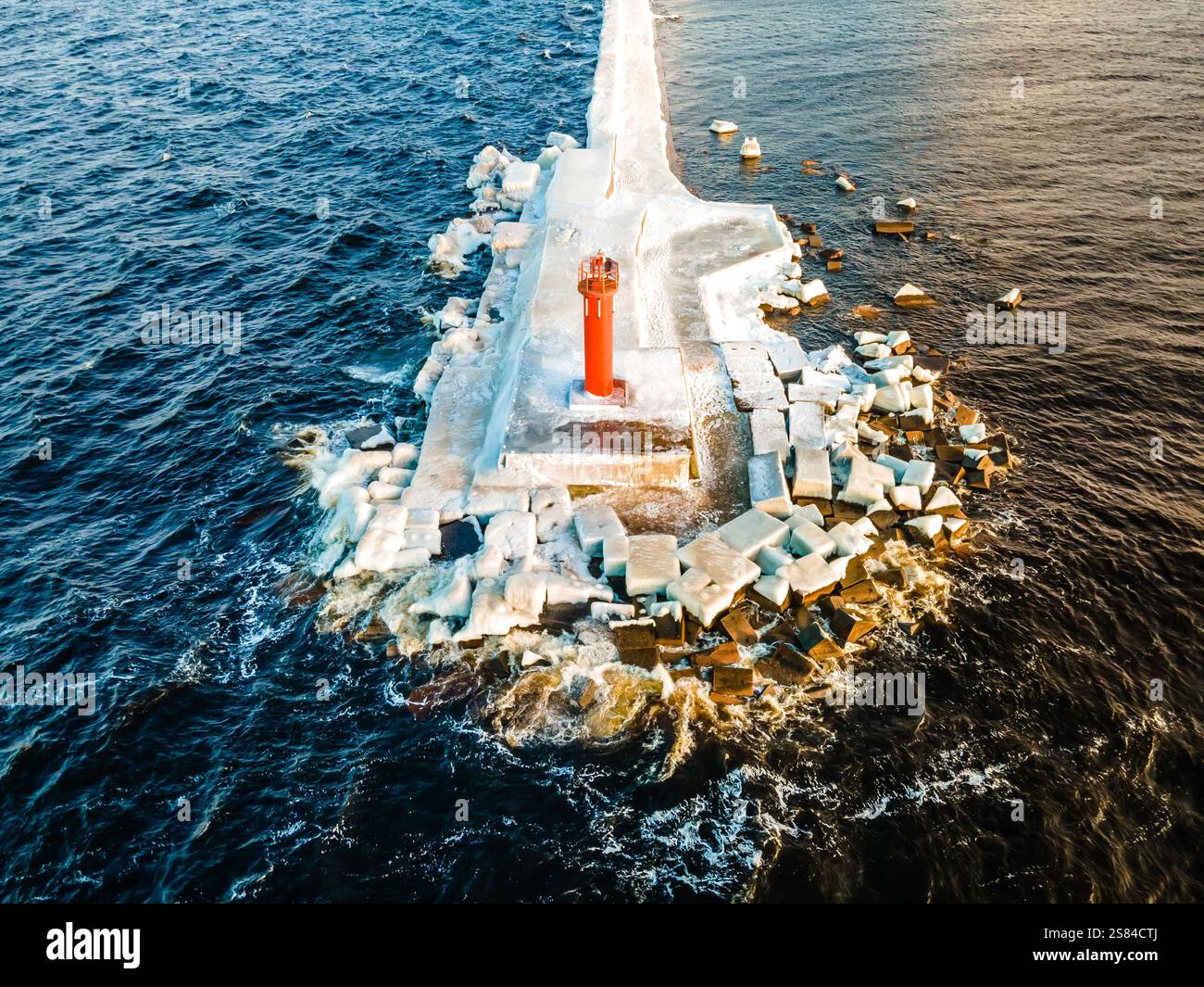 A vibrant red lighthouse stands on an icy pier surrounded by concrete ...