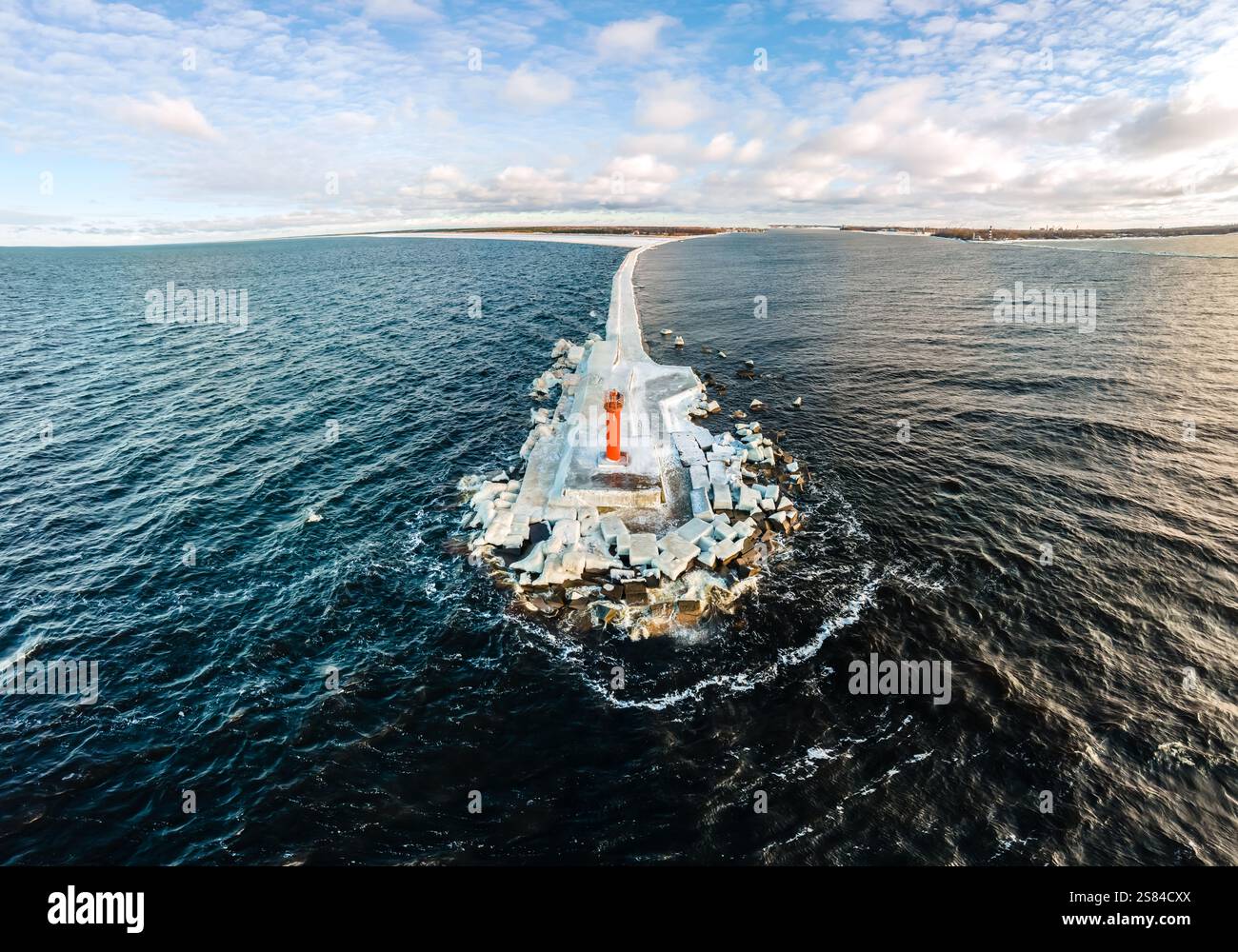 A vibrant red lighthouse stands on a narrow, icy pier surrounded by ...