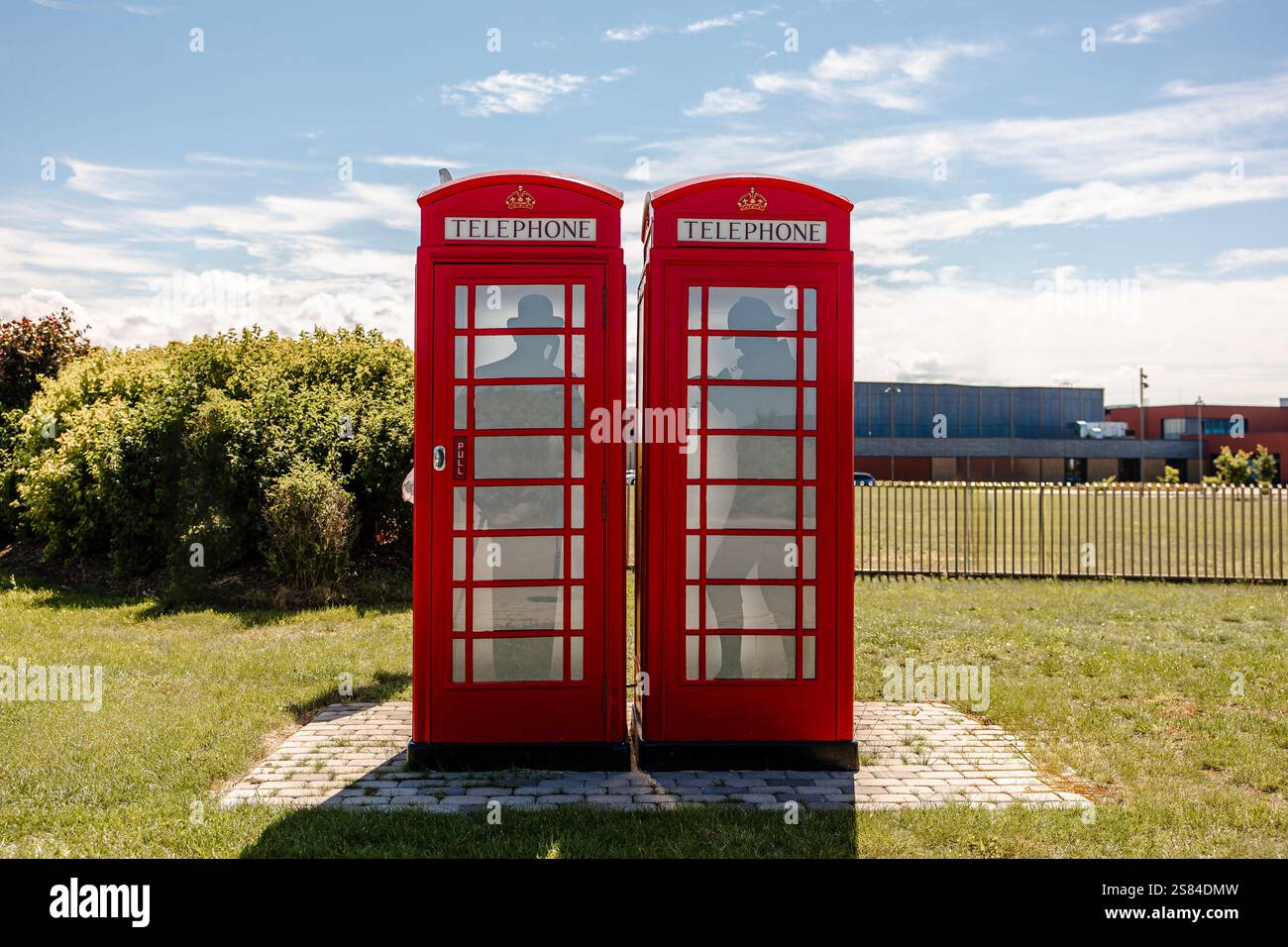 Two red British telephone booths with visible silhouettes stand on a ...
