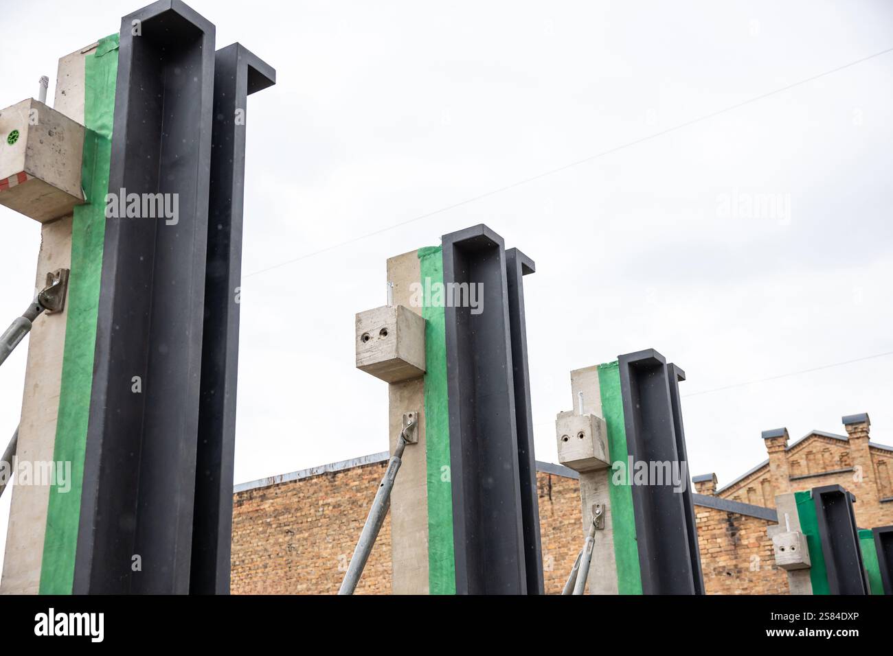 Vertical concrete and steel beams with green accents stand near a brick ...