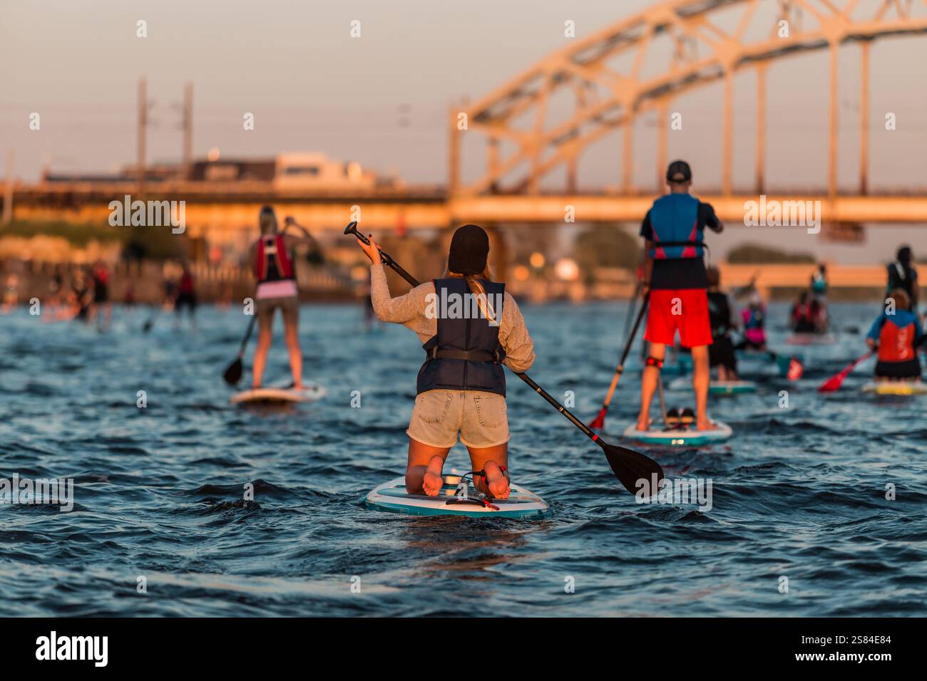 People paddleboard during golden hour under warm sunlight, with a train ...