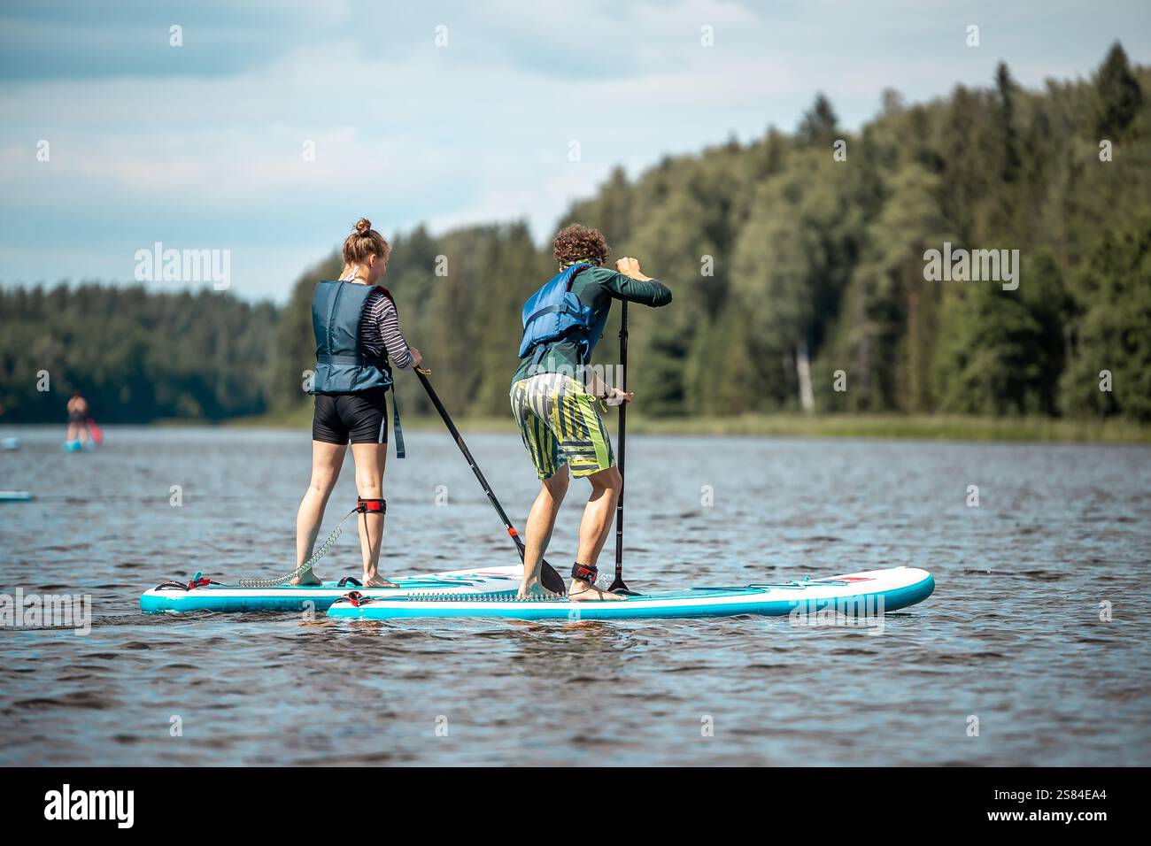 Two people paddleboard on a calm body of water, wearing safety gear. A ...