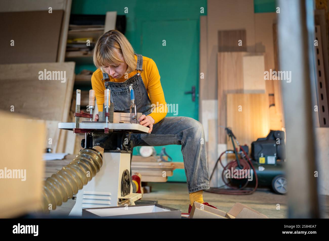 Female carpenter turn wood on lathe, shape custom pieces in workshop ...