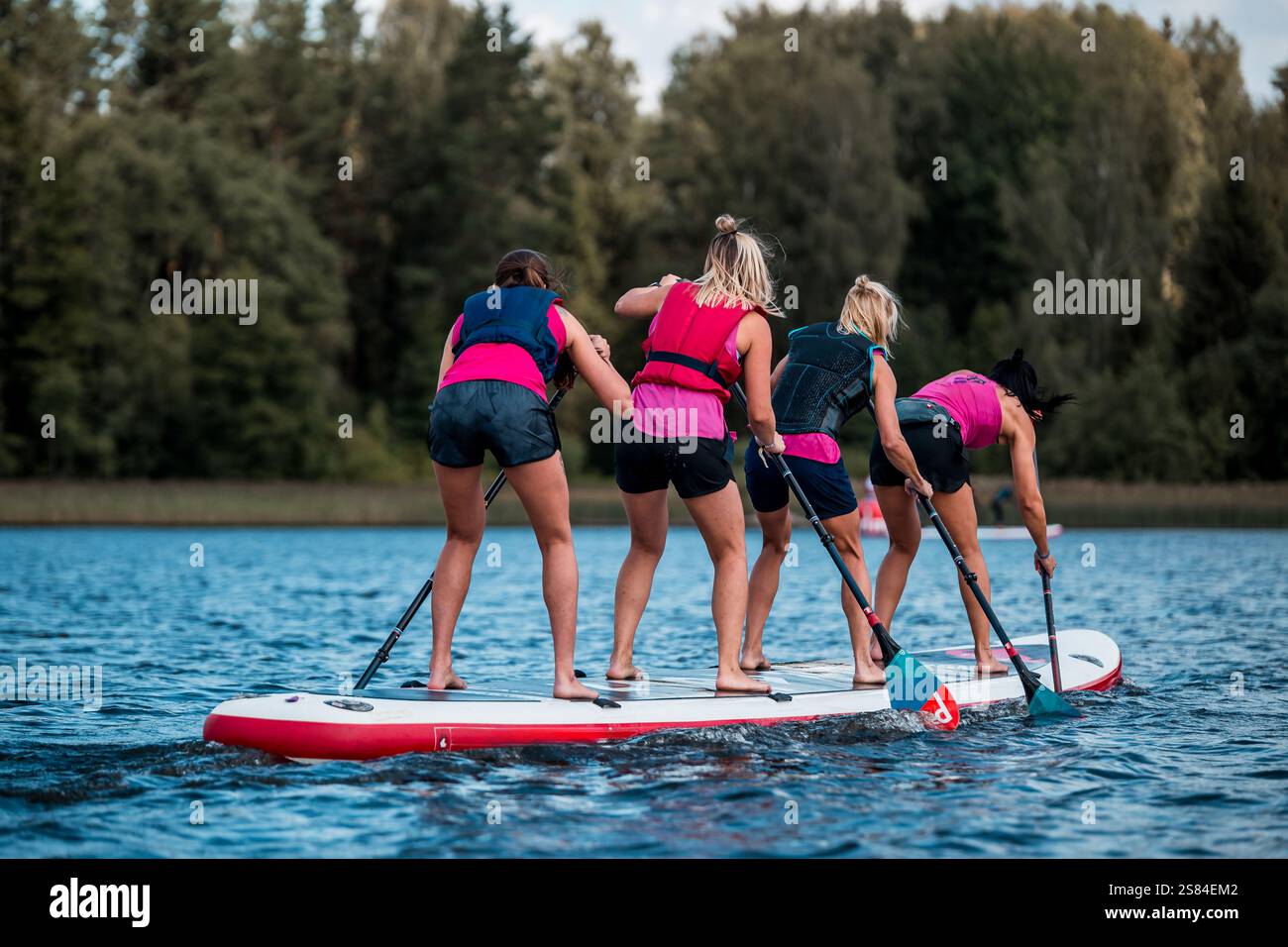Four people paddle together on a large board, wearing colorful life ...