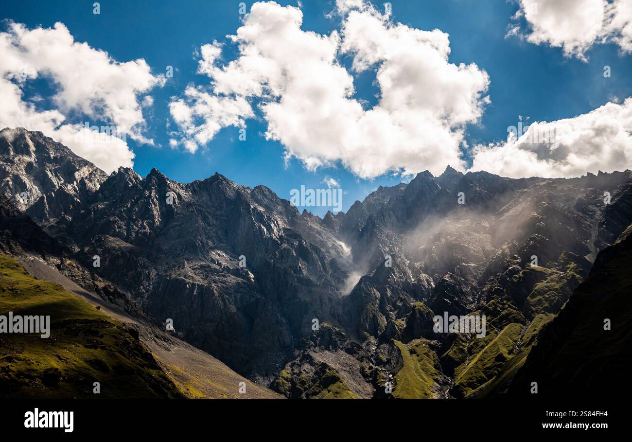 Rugged mountain peaks rise under a vibrant blue sky with scattered ...