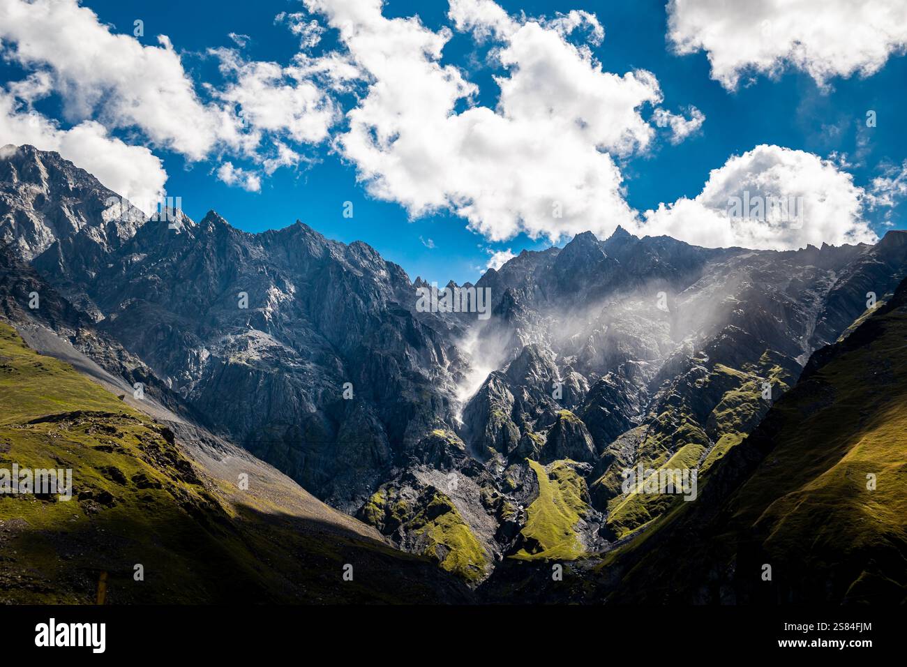 Rugged mountain peaks with steep rocky faces and green grass patches ...