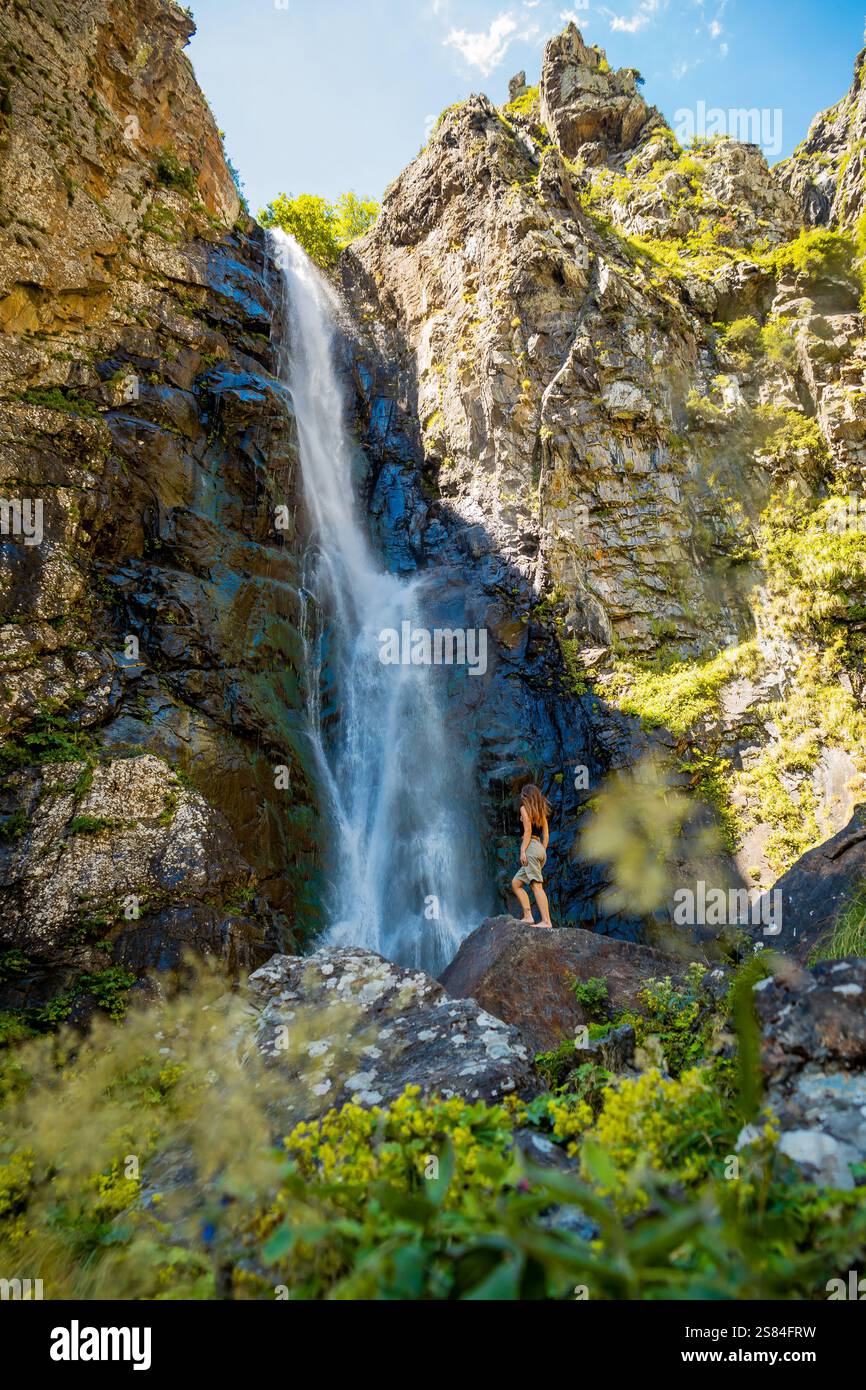 A waterfall flows down rugged cliffs surrounded by vibrant vegetation ...