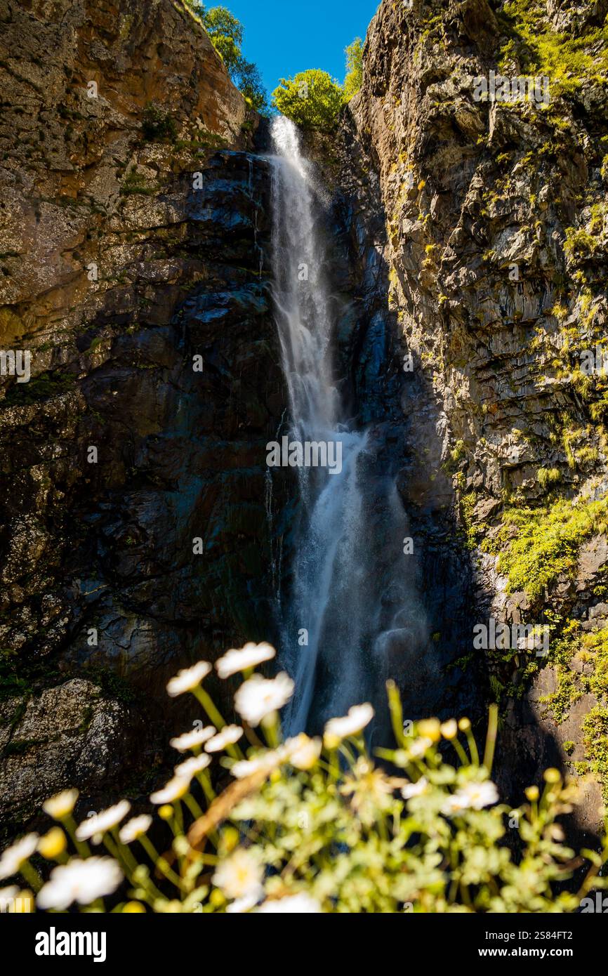 A waterfall cascades down rugged cliffs with green vegetation, framed ...