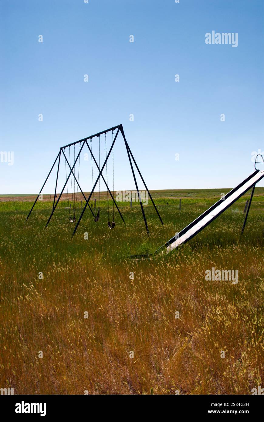 Abandoned swings and slide set on a vast grassy field under a clear ...
