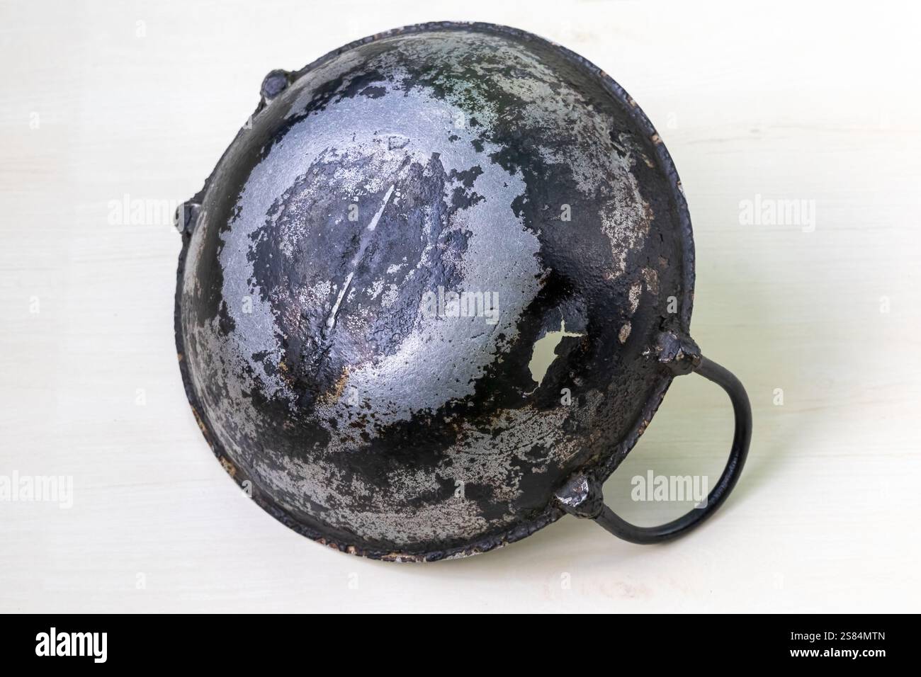 Back view of an old, iron karahi with holes, resting on a light wooden ...