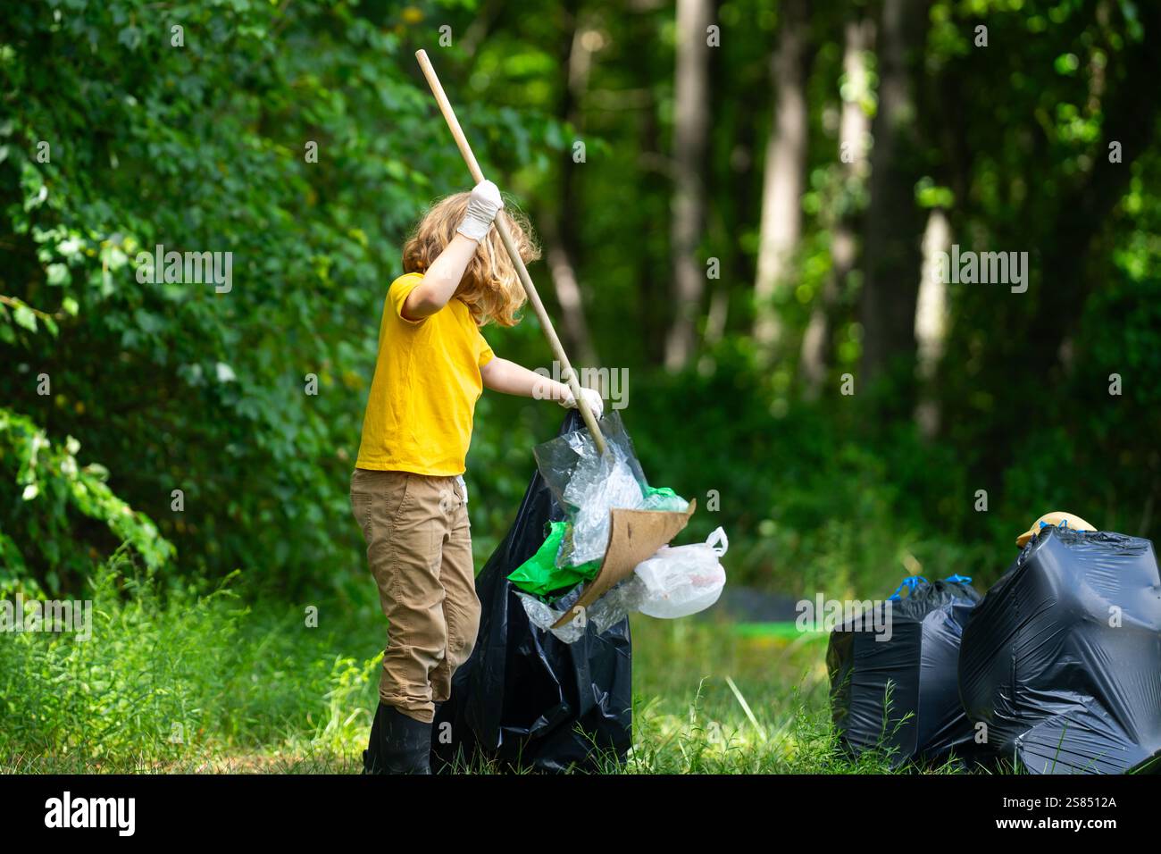 Kid cleaning up the park, putting trash in a garbage bag. Environmental ...