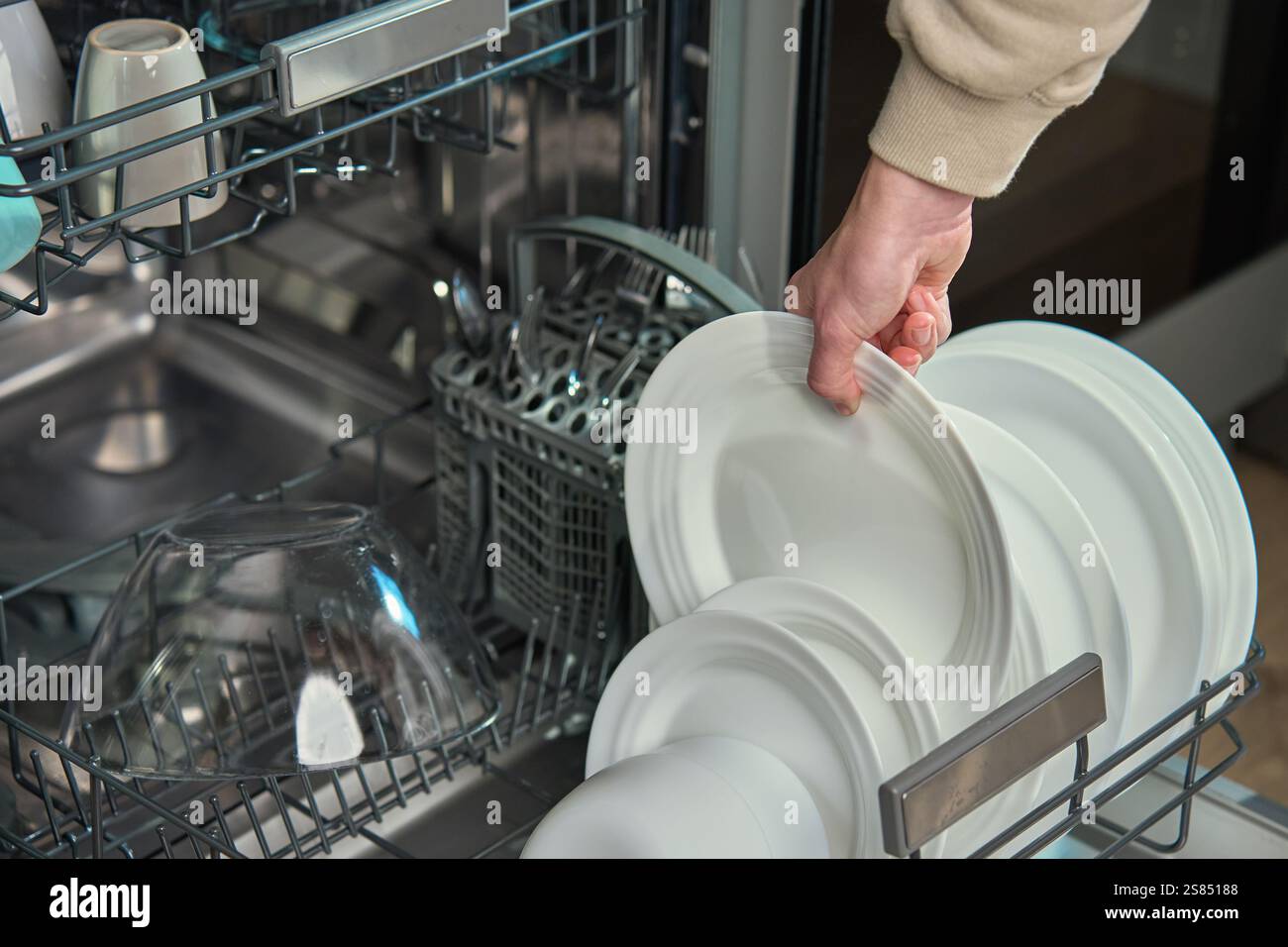 Woman unloading clean white plates from the bottom rack of dishwasher ...