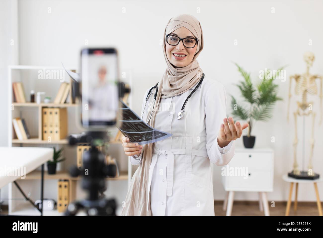 Muslim woman doctor recording video tutorial on x-ray treatment using smartphone. Middle Eastern ...