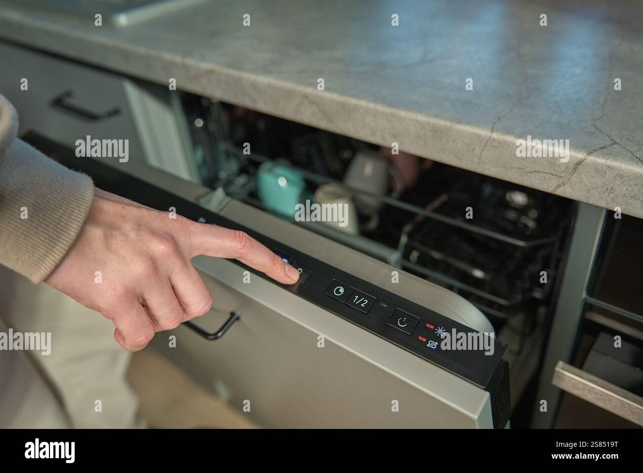 Hand pressing start button on dishwasher control panel with open door ...