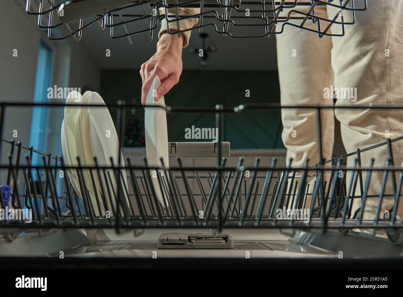 Woman unloading clean white plates from the bottom rack of dishwasher ...