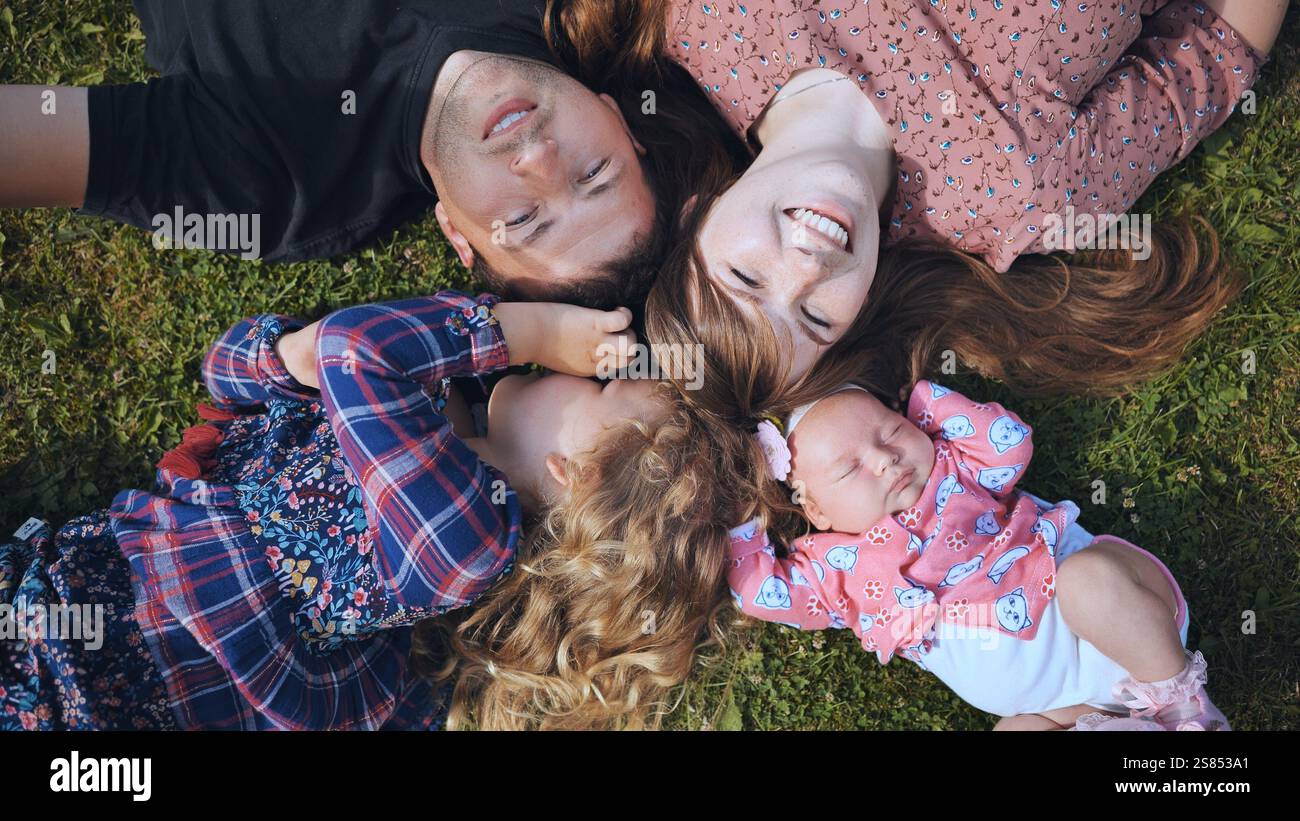 Loving parents cuddling with three daughters, relaxing on verdant lawn ...