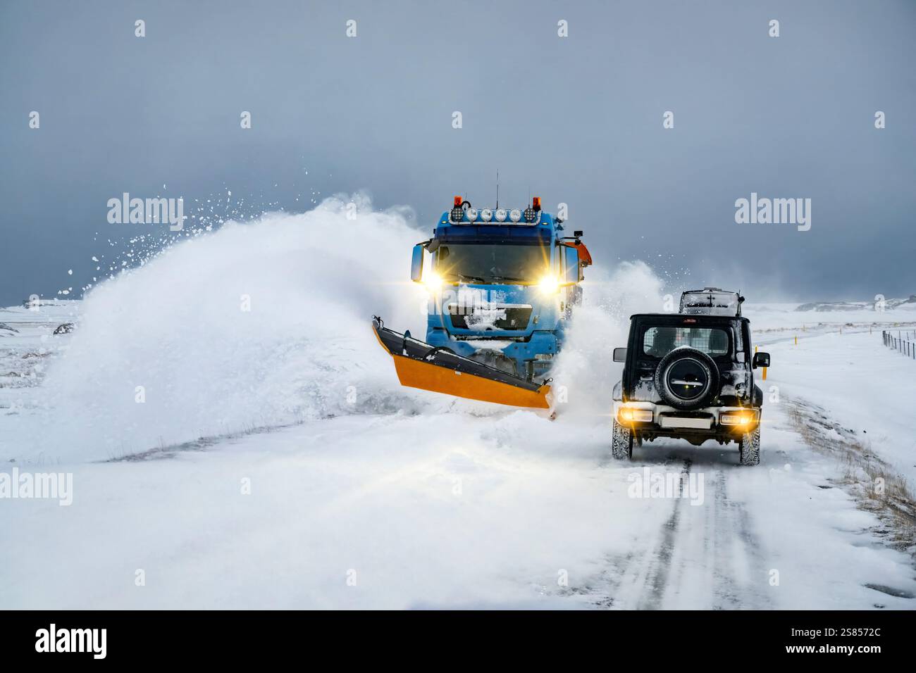 Car driving through a snow plow truck clearing snow from the road after ...