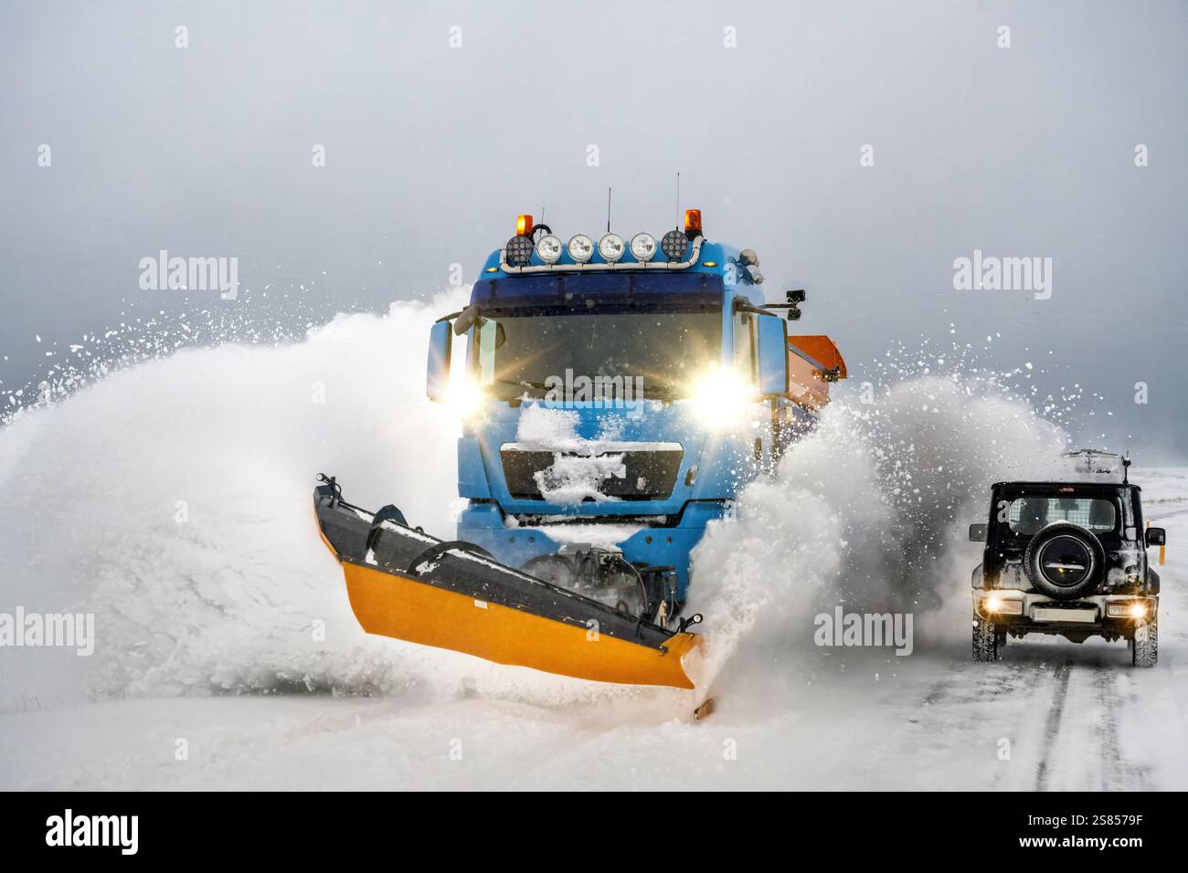 Car driving through a snow plow truck clearing snow from the road after ...