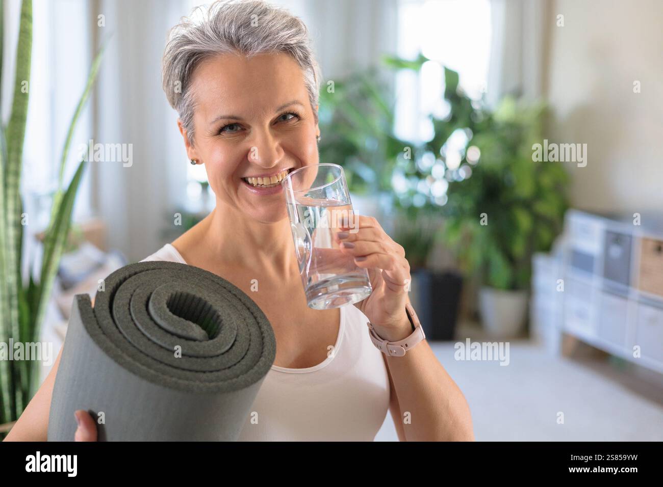 A mature woman of age with gray hair smiles and holds a glass with ...