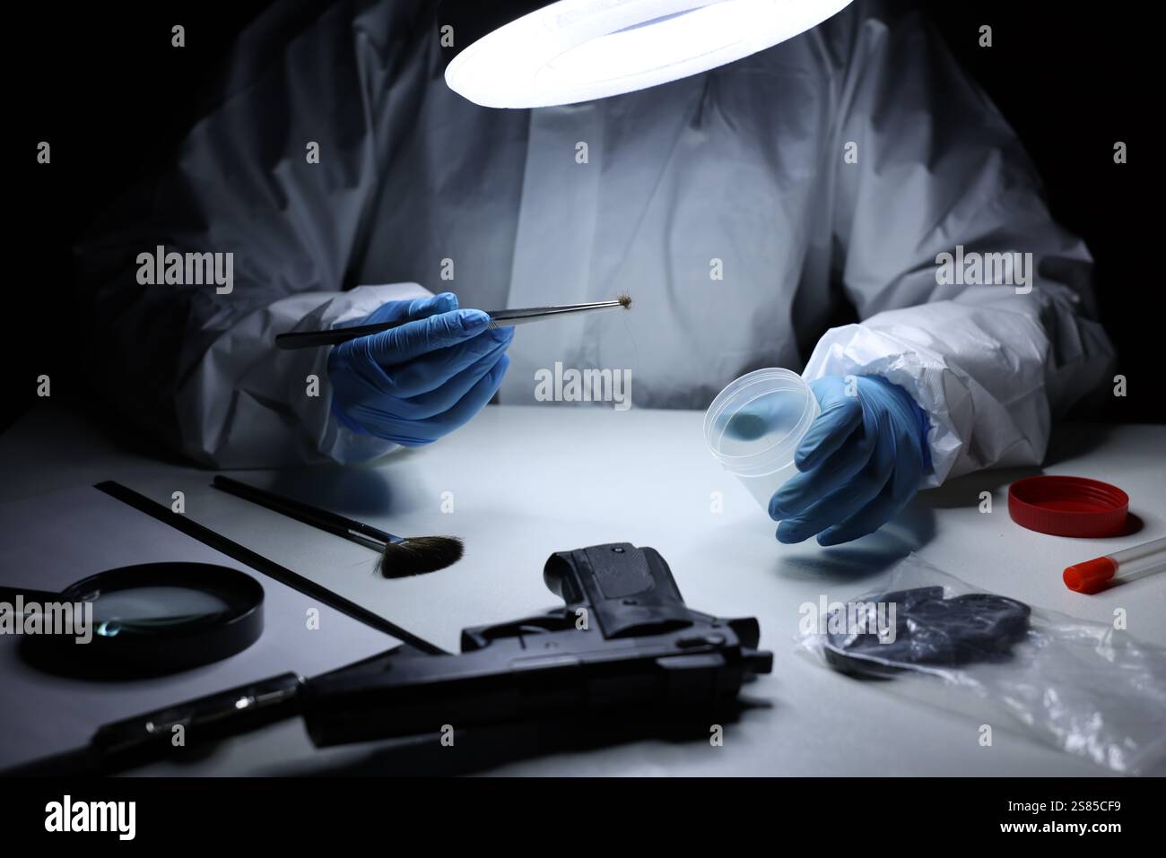 Forensic expert holding tweezers with hair sample and plastic container ...