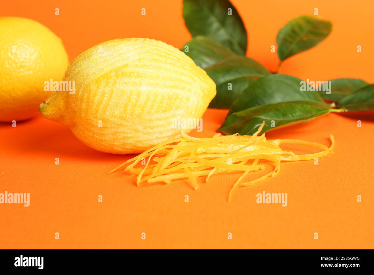 Lemon zest, fresh fruits and leaves on orange background, closeup Stock ...