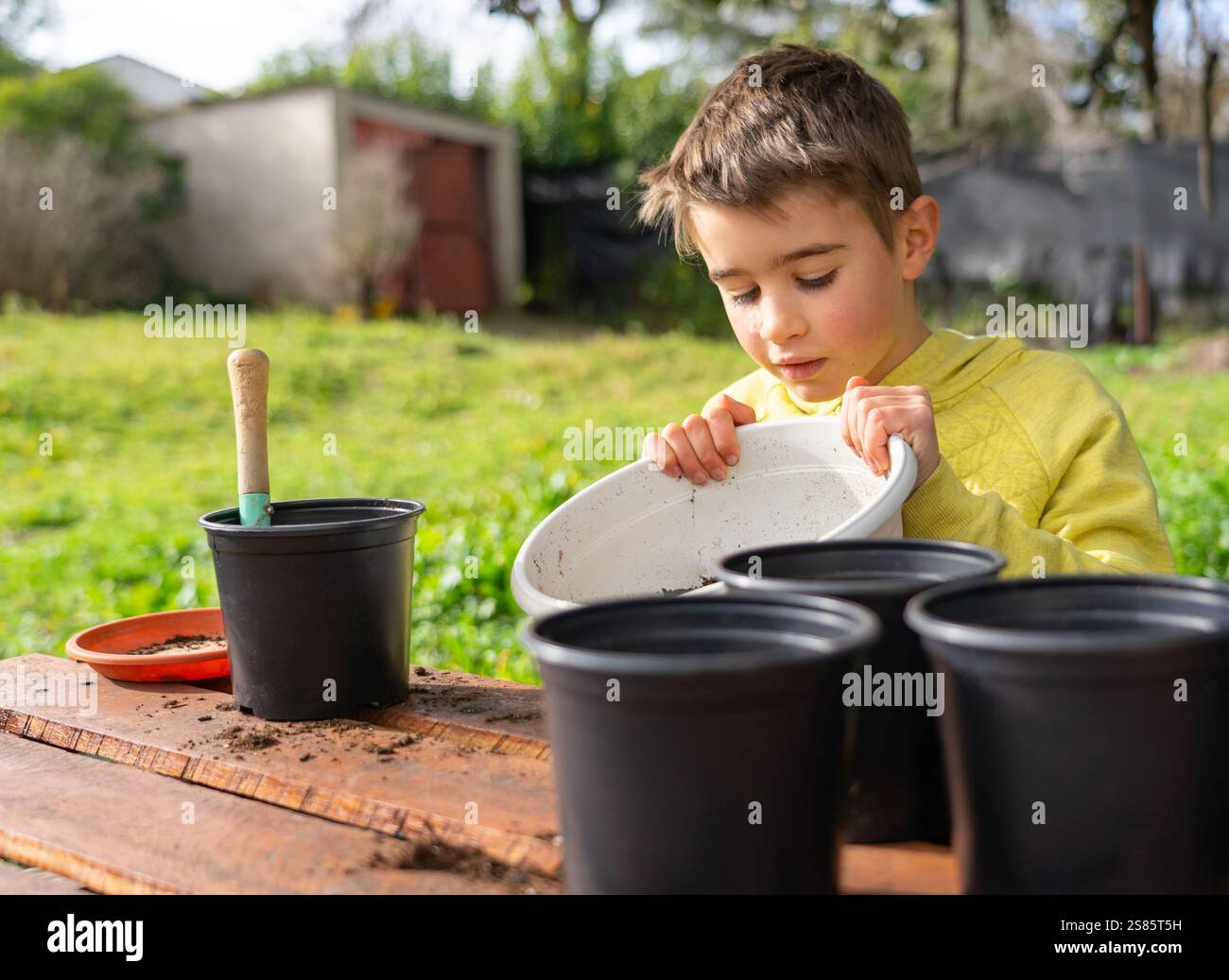 Child gardening, pouring soil into pots, preparing for planting Stock ...