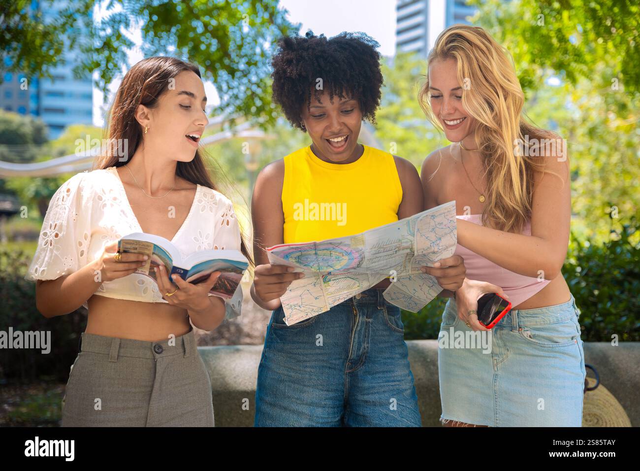 Three young women exploring a city with maps and a travel guide ...