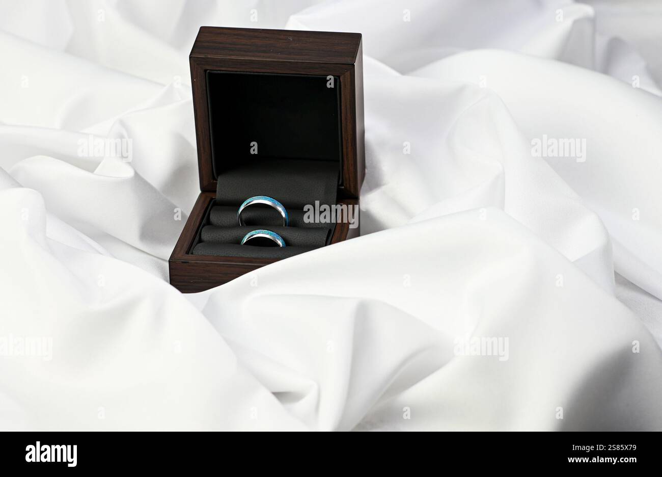 Wedding rings with turquoise enamel inlay are nestled in a dark wooden ...