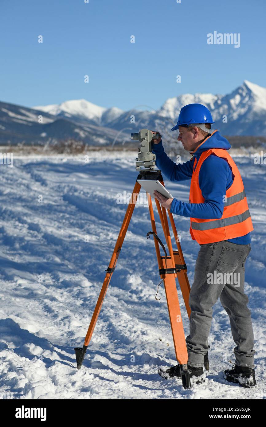 Surveyor taking measurements in snowy mountain landscape using ...