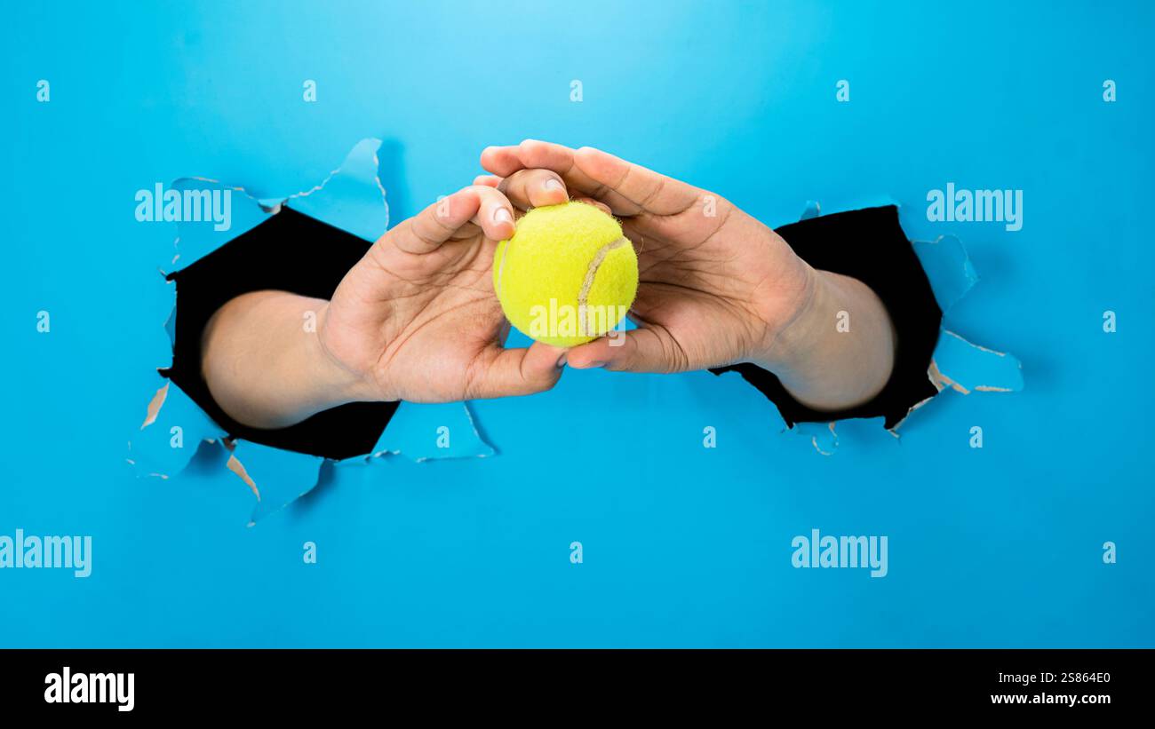 Human hand holding tennis ball through ripped paper. Mockup or Copy ...