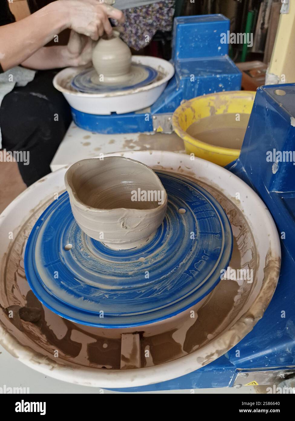 Pottery workshop scene with two pottery wheels in action. Un unfinished ...