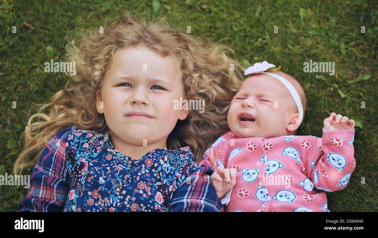Two sisters are lying on grass, the younger one crying and the older ...