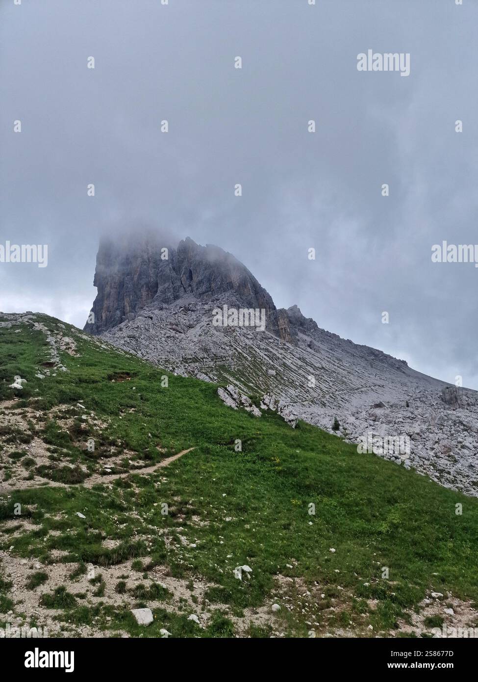 Dramatic mountain peak partially shrouded in mist, set against a cloudy ...