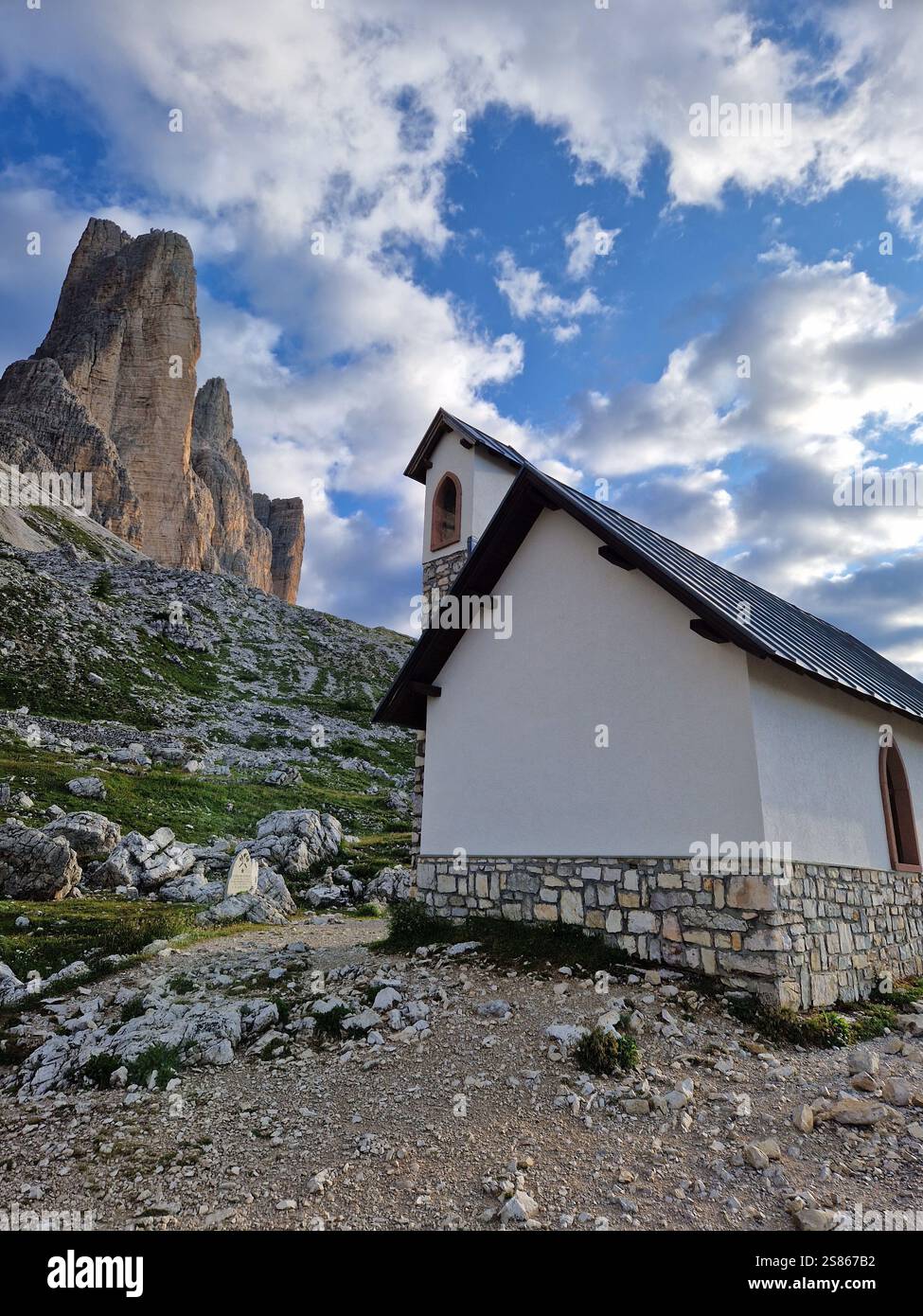 A chapel against towering rugged peaks in the Italian Dolomites, hiking ...