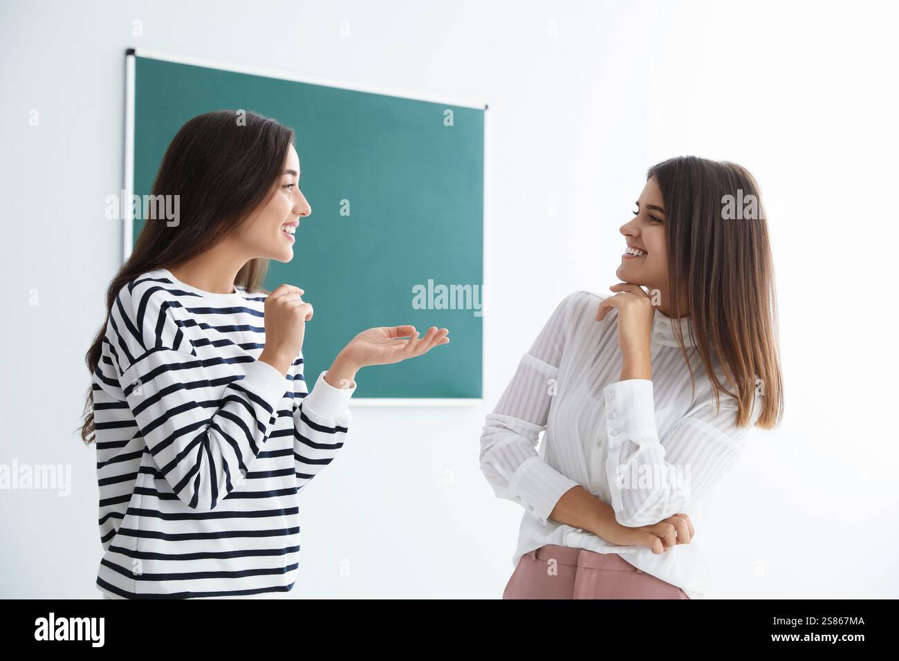 Young women talking near green chalkboard in classroom Stock Photo - Alamy