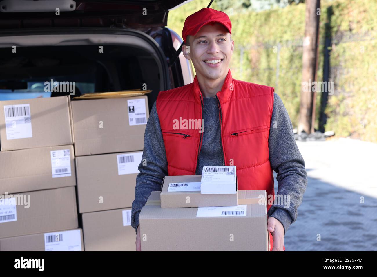 Happy postman with parcels near car outdoors Stock Photo - Alamy