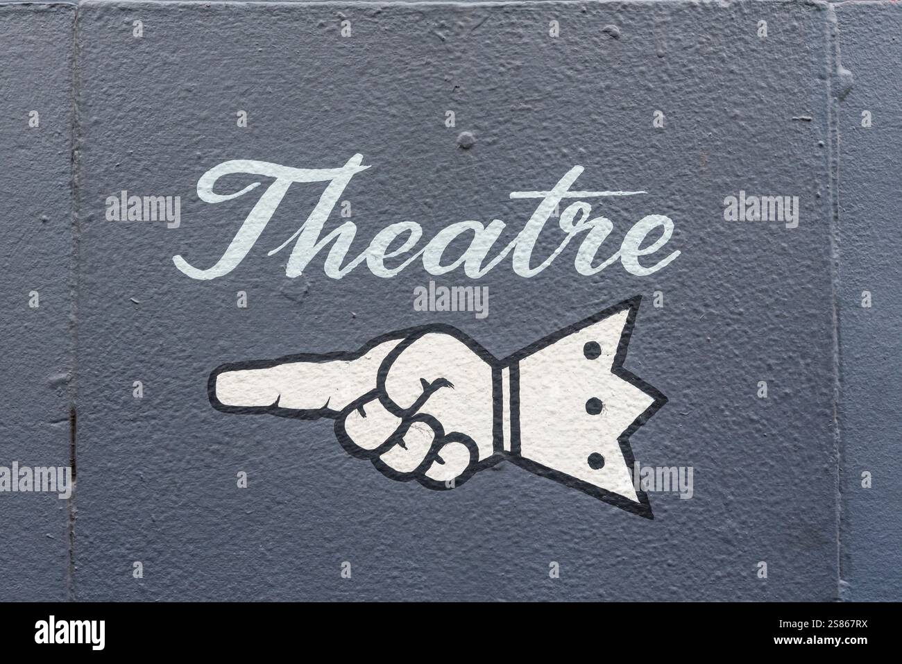 A hand painted sign on a concrete wall pointing to a theatre. A very ...