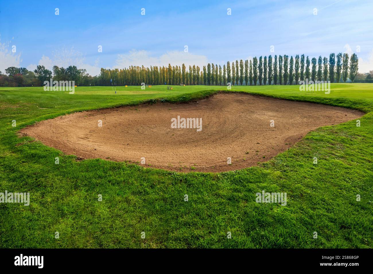 Large sand bunker on a lush green golf course under a clear blue sky ...