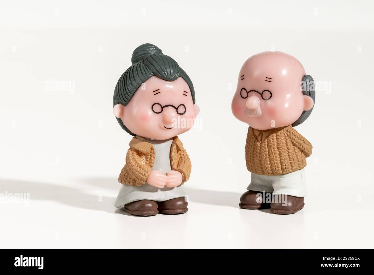 Two cute cartoon figurines of an old man and woman wearing glasses and sweaters, representing an ...