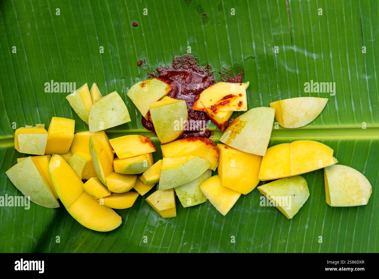 Mango cut into pieces served on banana leaf with red chilly paste in ...