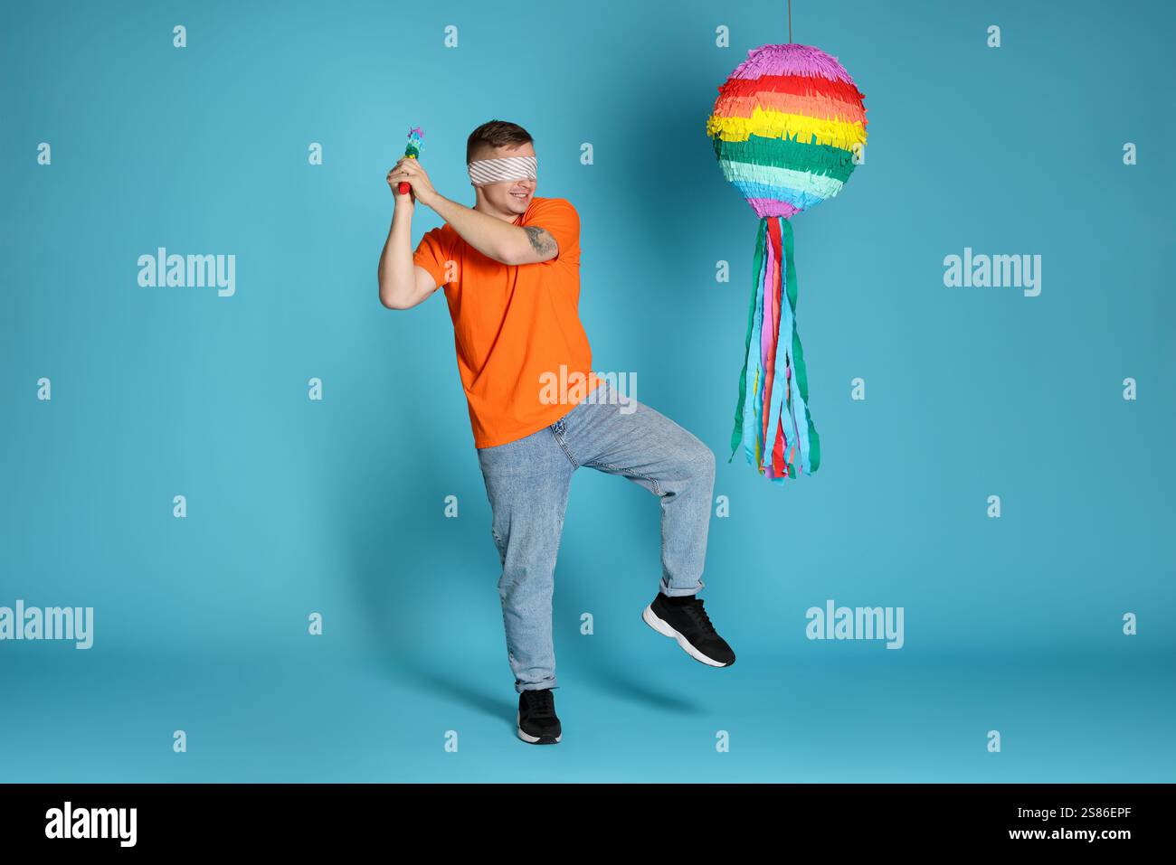 Man with tied eyes breaking pinata on light blue background Stock Photo ...