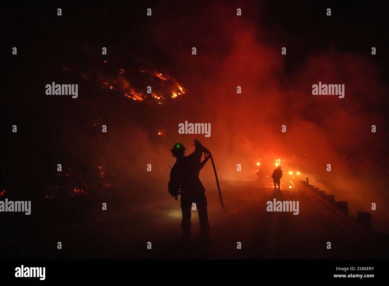 Two firefighters roll up a fire hose during the Lilac Fire in Bonsall ...